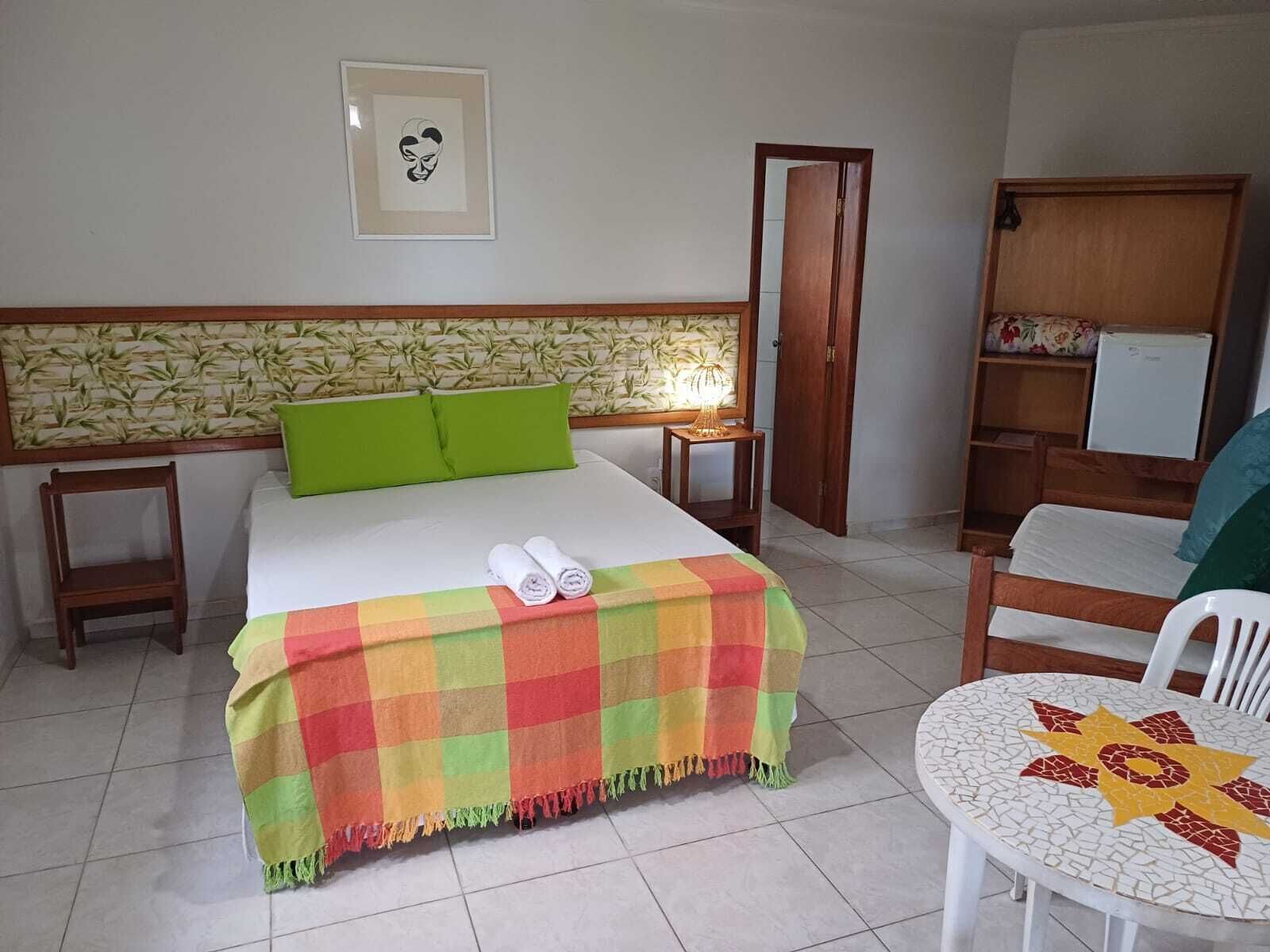 Quarto de hotel com uma cama, uma cadeira, uma mesinha e um guarda-roupa.