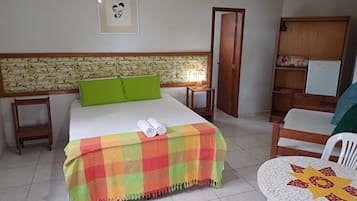 Quarto de hotel com uma cama, uma cadeira, uma mesinha e um guarda-roupa.