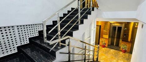 Uma escadaria com corrimão de metal, degraus pretos e parede branca com design vazado.
