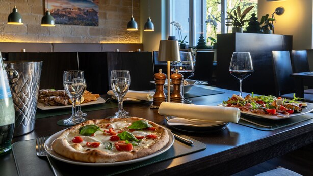Um ambiente de restaurante com pizza, salada e copos de vinho sobre a mesa.