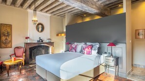 Um quarto espaçoso com uma cama grande, lareira, candelabro e uma cadeira vermelha.