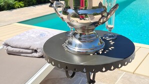 Uma garrafa de champanhe prateada em suporte decorativo, à beira da piscina.