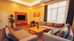 Uma sala de estar moderna com sofá, mesa de centro, TV na parede e uma grande janela com cortinas.