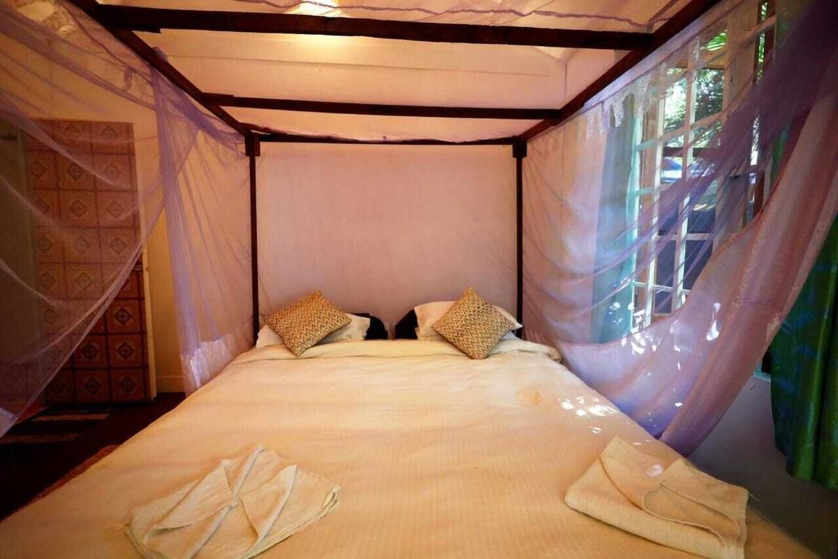 Uma cama de solteiro com dossel, duas almofadas e um par de toalhas no chão.