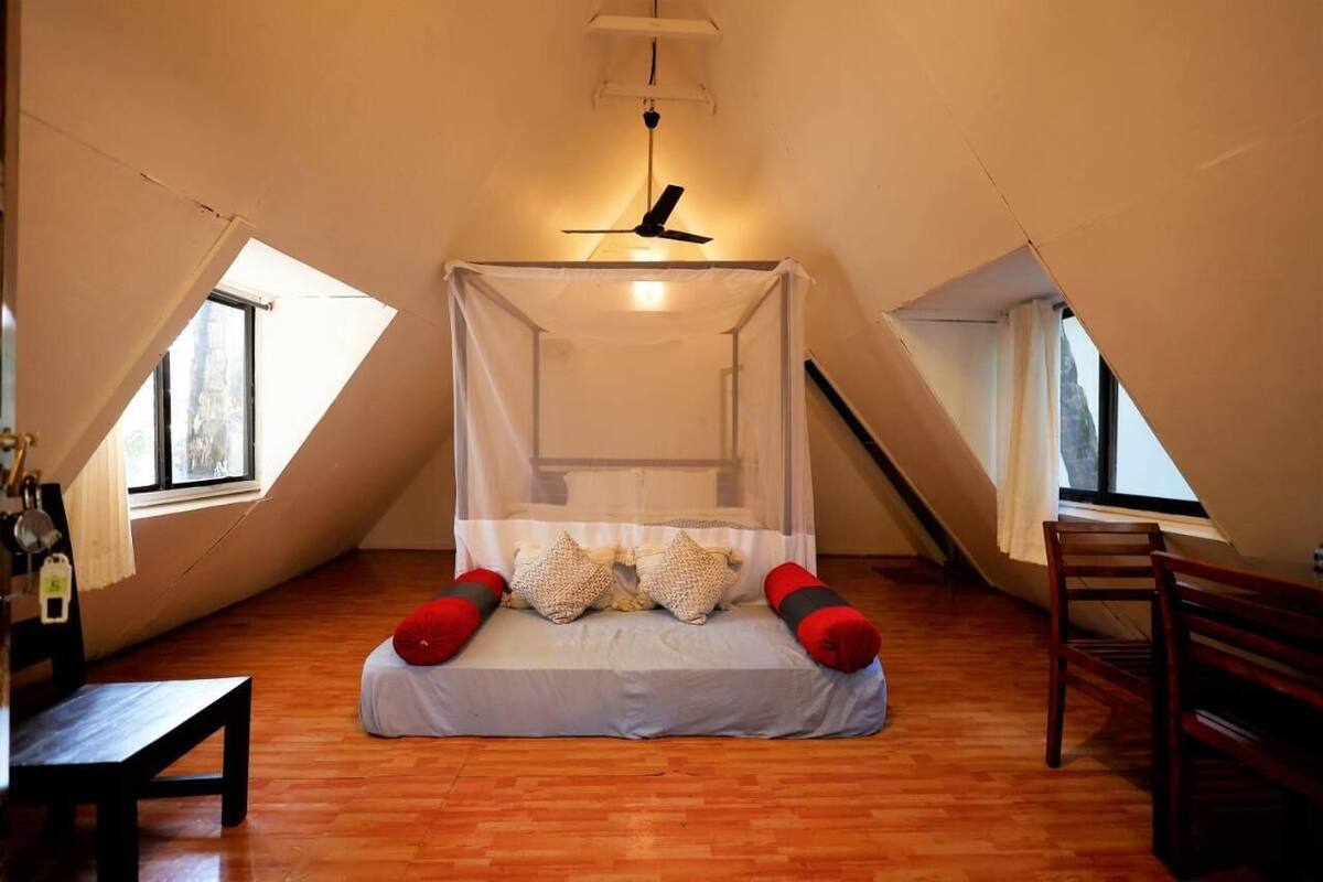 Quarto com cama de dossel, piso de madeira e duas janelas.