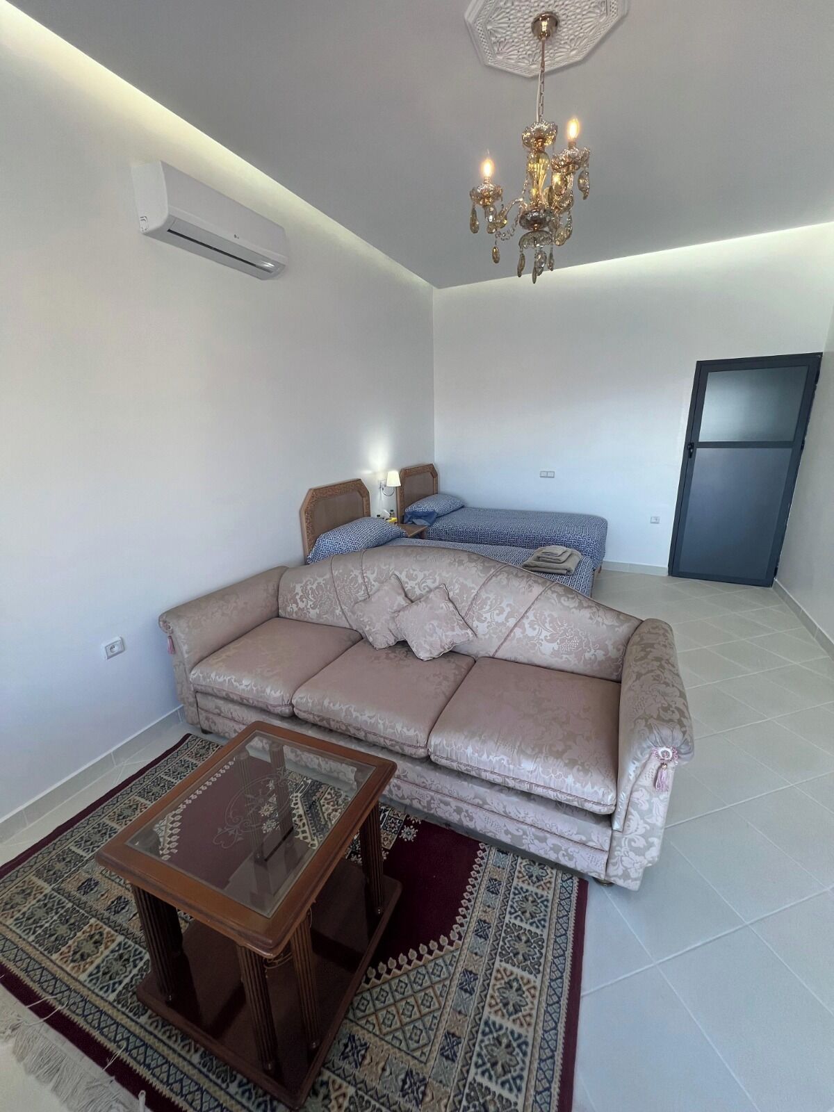 Uma sala de estar moderna com um sofá bege, mesa de centro de madeira, tapetes estampados e um candelabro.