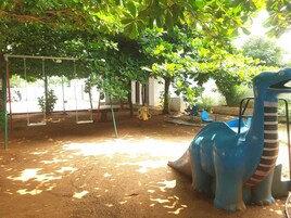 Um parquinho com balanços e uma escultura de dinossauro azul.