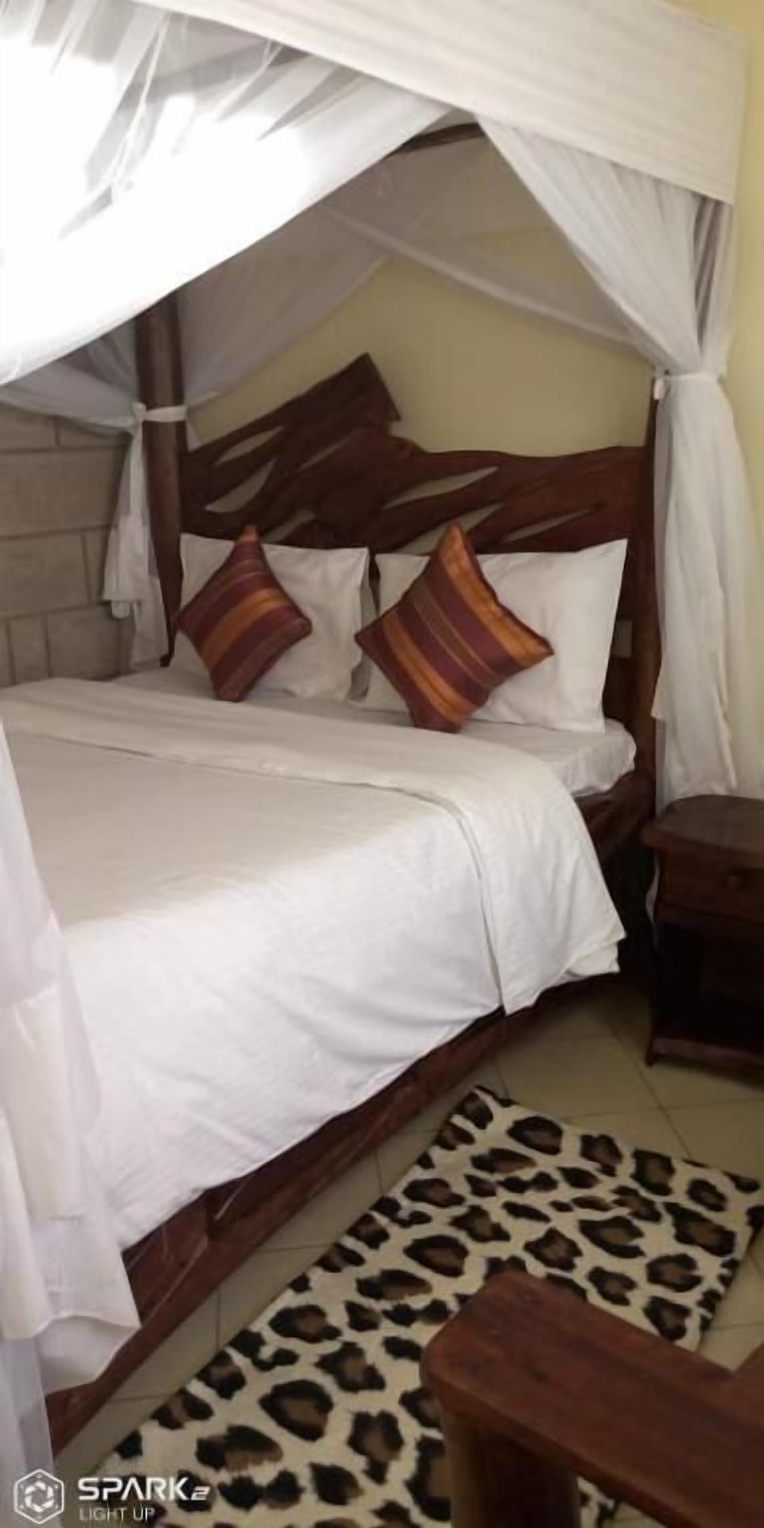 Uma cama com cabeceira de madeira, roupa de cama branca e almofadas listradas. Há uma pequena mesa de cabeceira ao lado da cama.