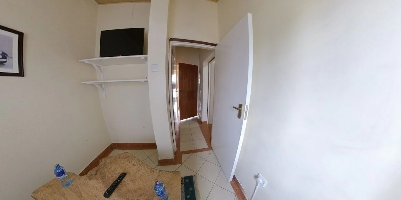 Quarto com carpete bege, uma garrafa de água, um controle remoto e uma TV em uma estante.