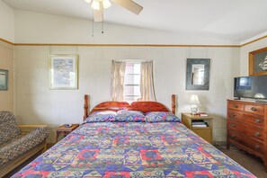 Quarto com cama, cómoda de madeira, mesa de cabeceira, cadeira e ventoinha no teto.