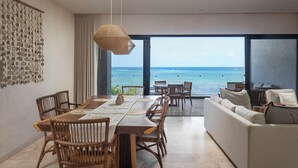 Uma área de refeições moderna com vista para o oceano, apresentando uma mesa de madeira, cadeiras de vime e uma janela grande.