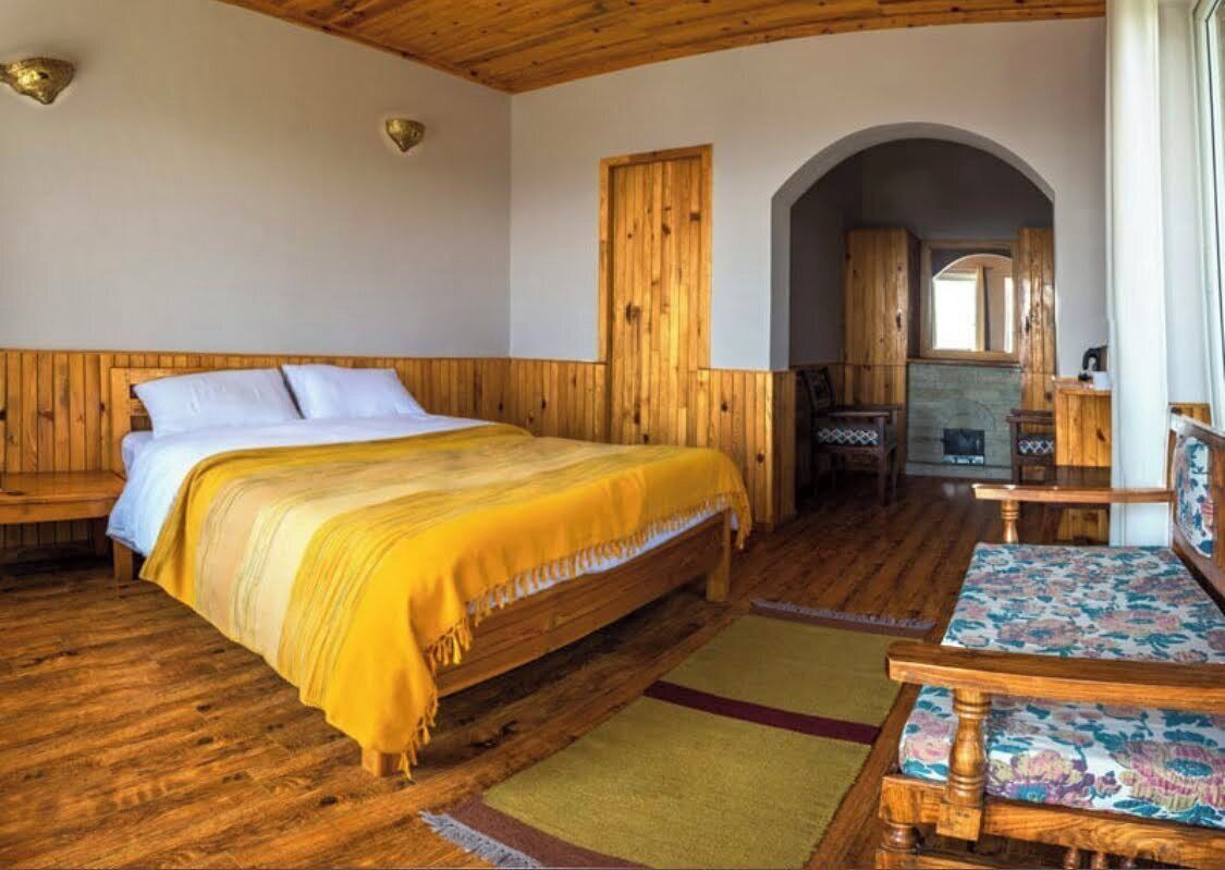 Um quarto de madeira com uma cama, um banco de madeira, uma mesa e uma cadeira.
