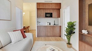 Uma sala de estar moderna com sofá, mesa de centro e cozinha com armários de madeira e micro-ondas.