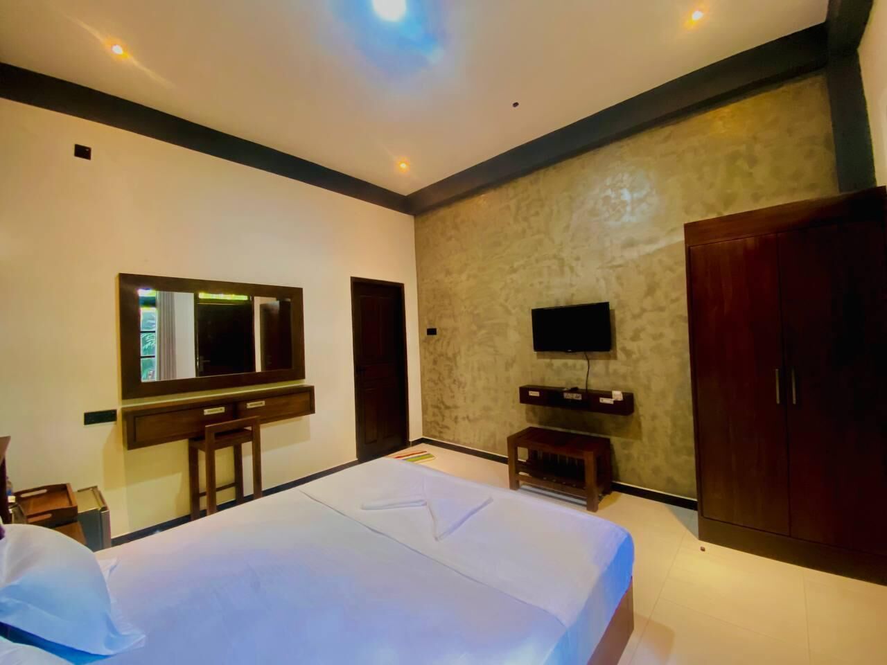 Quarto de hotel com uma cama grande, televisão fixada na parede e um guarda-roupa.