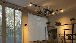Um restaurante com mesas internas, uma tela de projeção e diversos vasos de plantas.