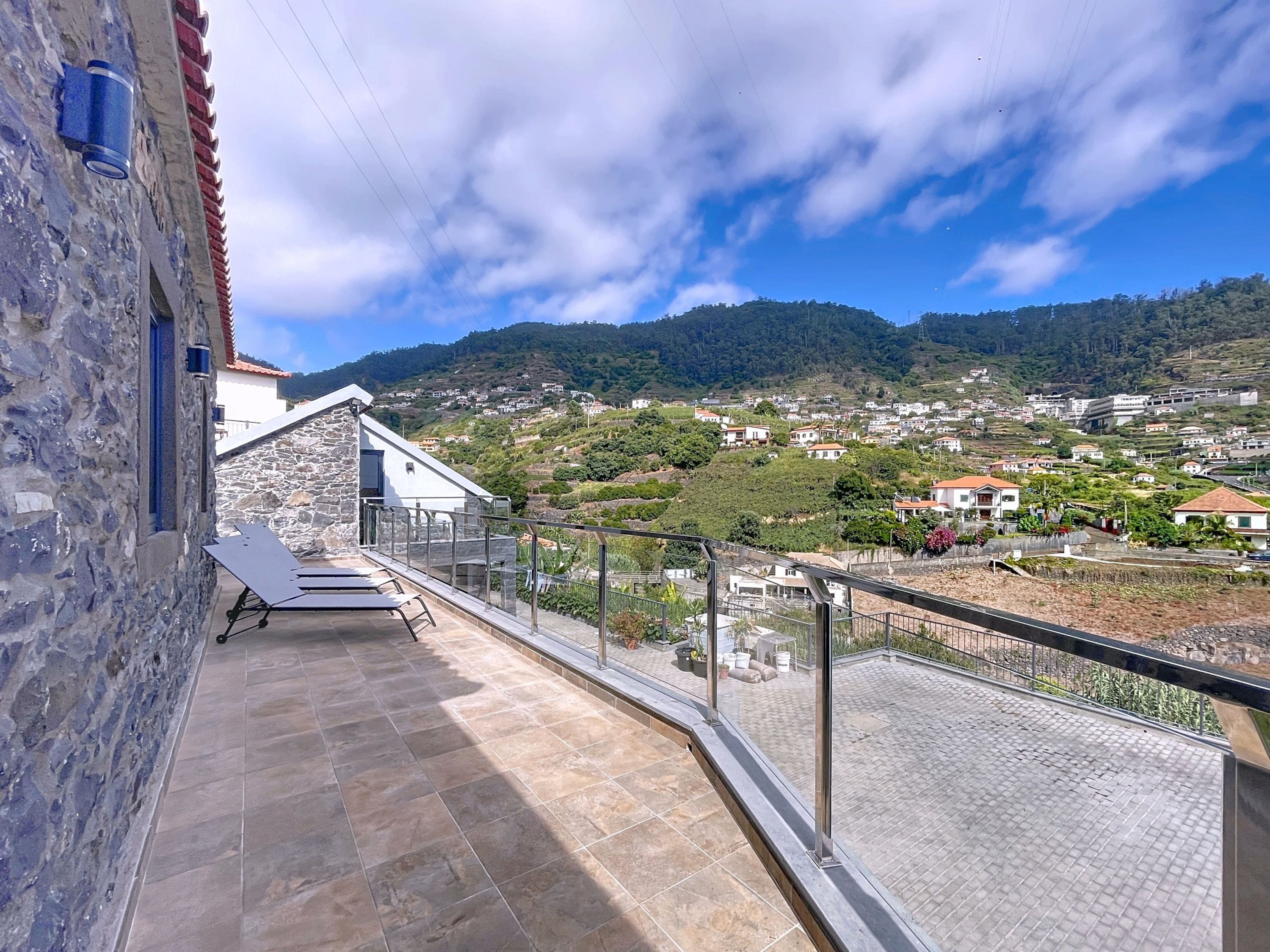 Uma varanda com parede de pedra, guarda-corpo de vidro e vista para uma cidade no morro.