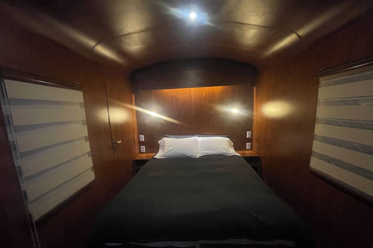Um quarto pequeno e mal iluminado, com uma cama, paredes de madeira e teto inclinado.
