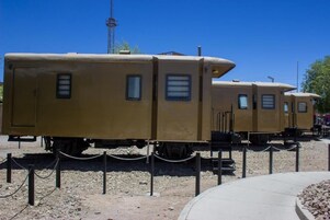 Uma fileira de carros de trem antigos em exposição, cada um com uma pequena janela e uma barreira de corrente na frente.