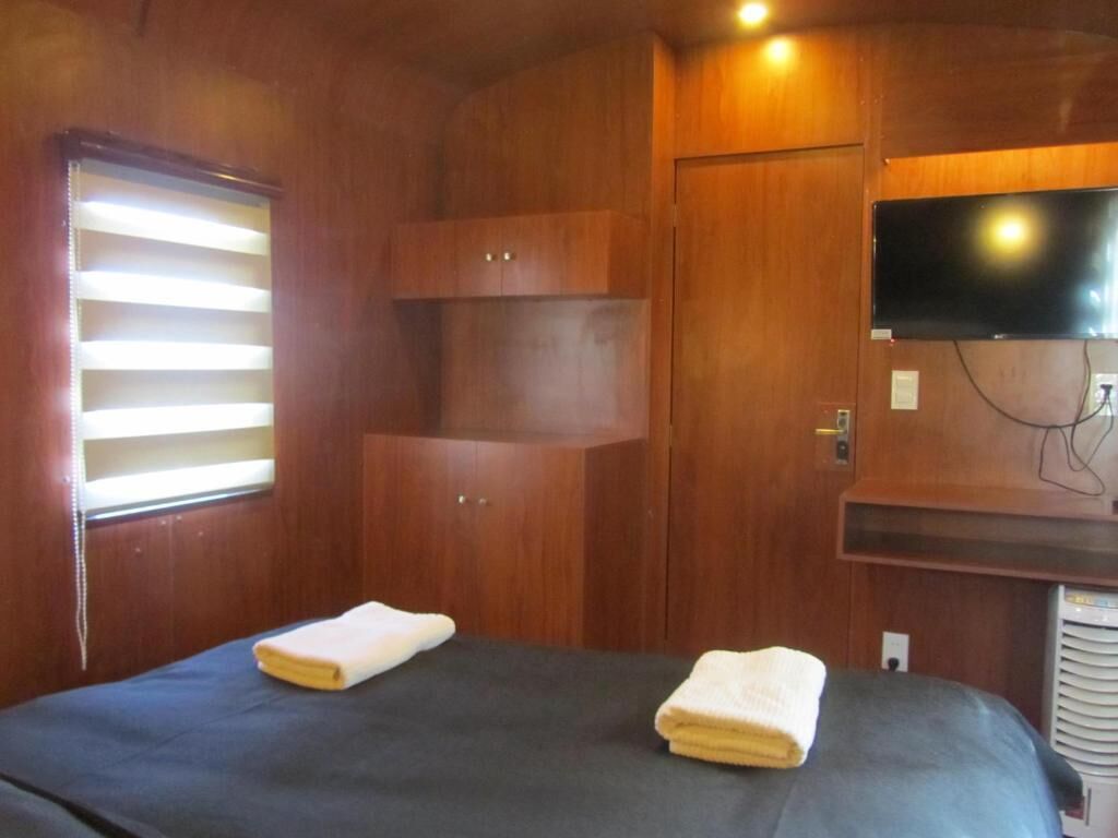Quarto com cama, televisão fixada na parede e janela com persianas.