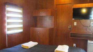 Quarto com cama, televisão fixada na parede e janela com persianas.
