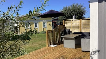 Um deck de madeira com móveis externos, uma pérgula e vista para uma casa.