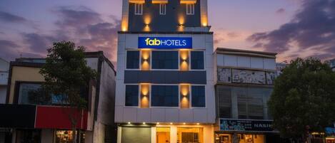 Um edifício moderno com a placa 'fab hotels', apresentando uma estrutura de vários andares com janelas iluminadas e um telhado plano.