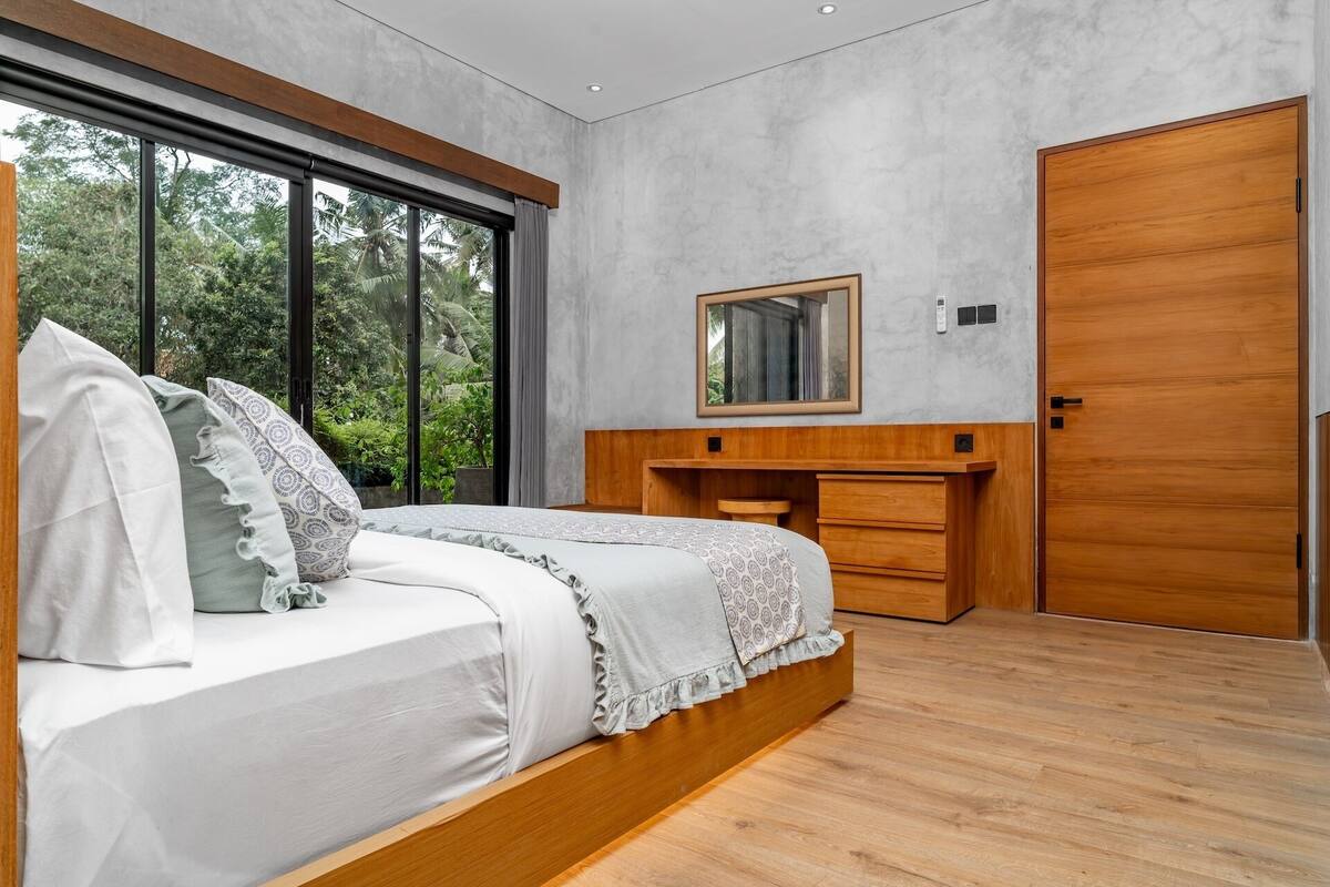 Um quarto moderno com uma cama grande, uma cômoda de madeira, um espelho e uma porta de madeira.