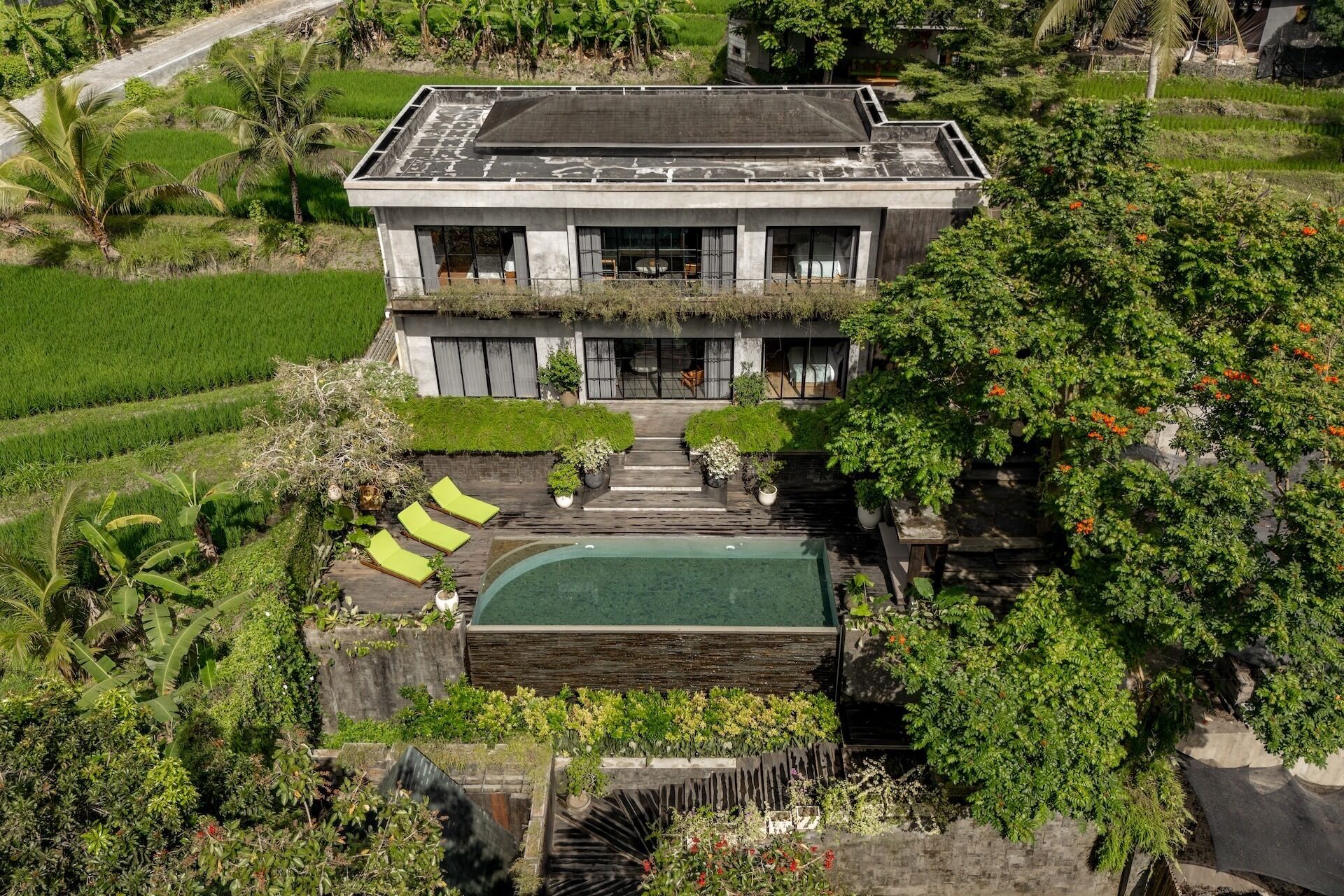 Uma casa moderna de dois andares com terraço no telhado, cercada por vegetação exuberante e uma piscina.