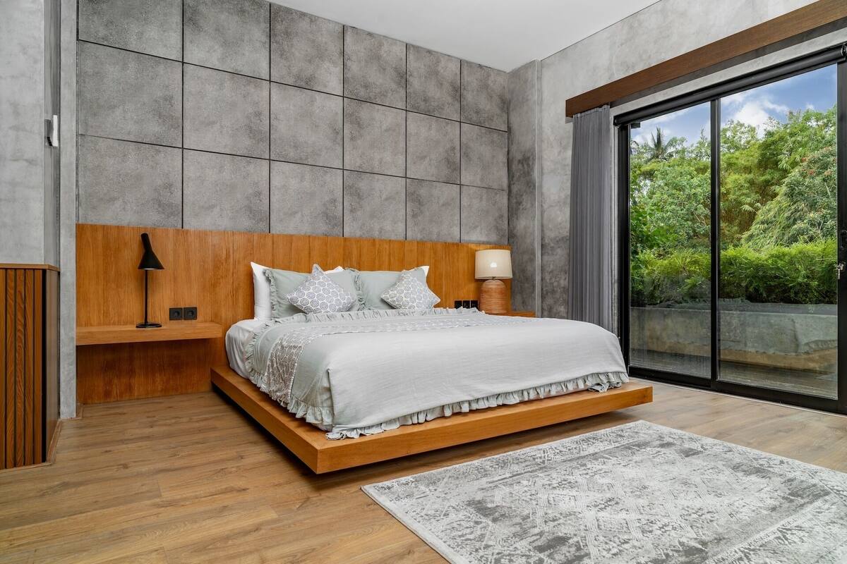 Quarto moderno com cama grande, cabeceira de madeira e vista para o verde através de uma porta de correr de vidro.