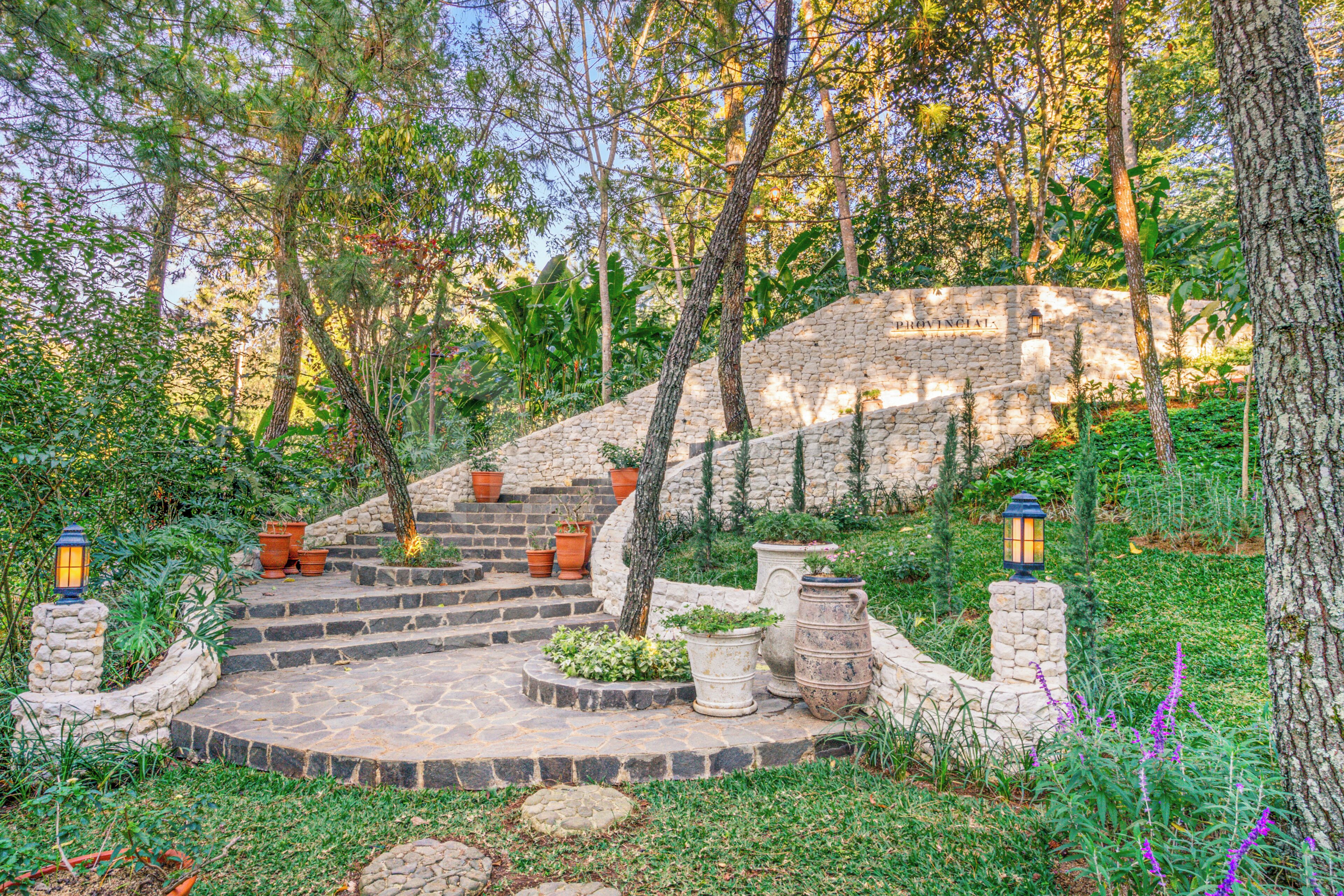 Uma escadaria de pedra rodeada por vegetação, com plantas em vasos e lanternas.