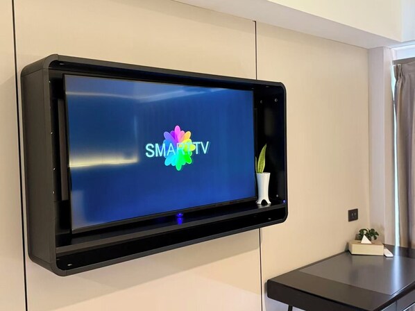 Uma televisão de tela plana fixada na parede, com o logotipo "SMARTTV" e uma planta decorativa ao lado.