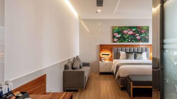 Quarto de hotel com cama, sofá, mesa de cabeceira com abajur e um quadro na parede.