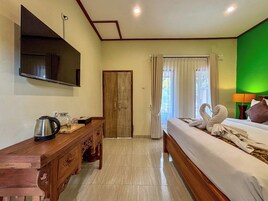 Quarto de hotel com cama, cómoda de madeira, televisão fixada na parede e uma parede de destaque verde.