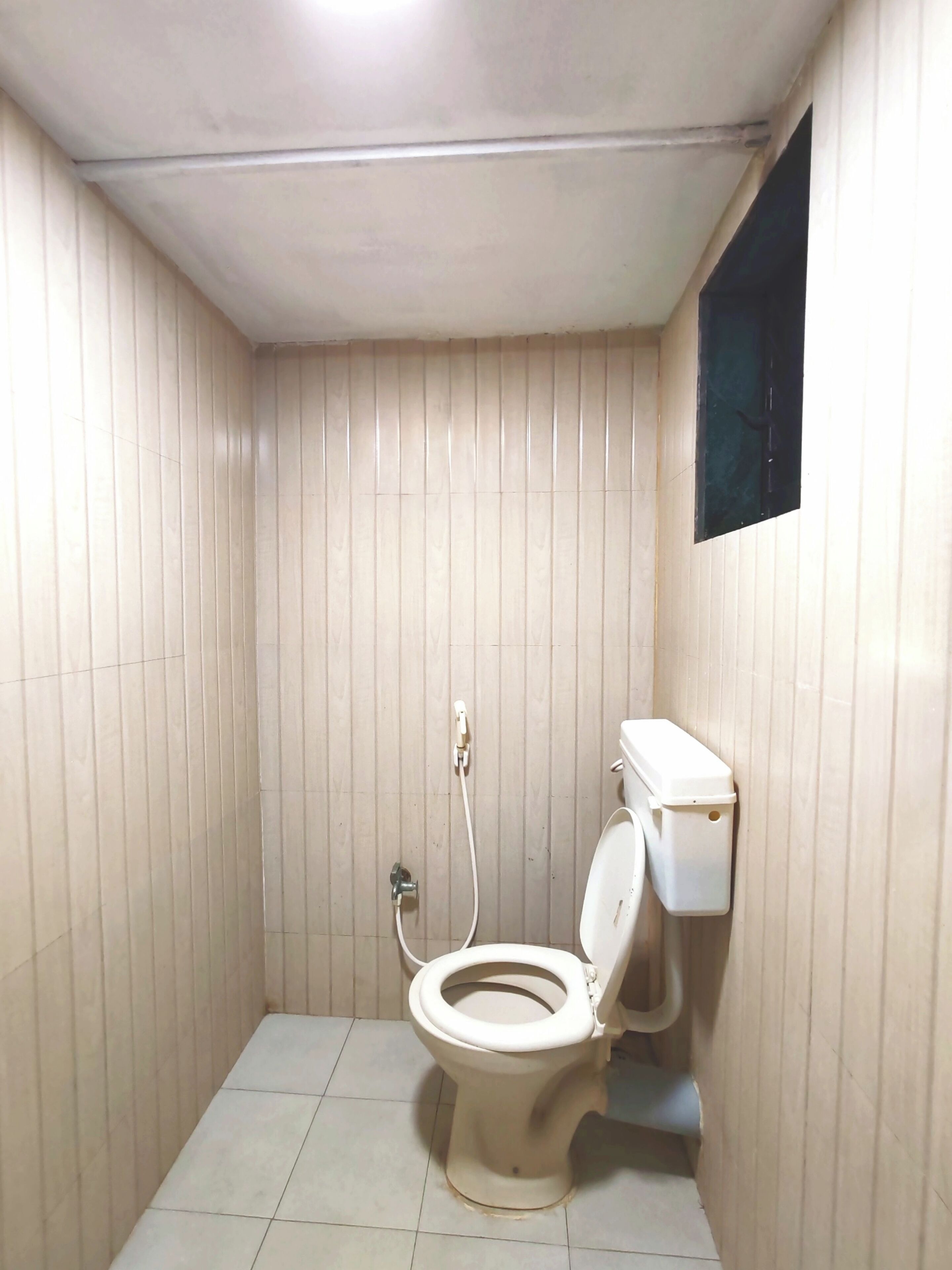 Um banheiro pequeno, com azulejos, que inclui vaso sanitário, chuveiro e janela.