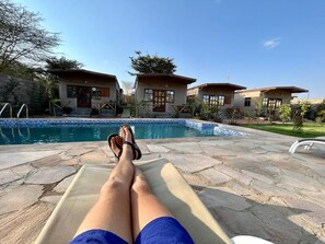 Vista da piscina com espreguiçadeiras, piscina e um edifício com fachada de pedra.
