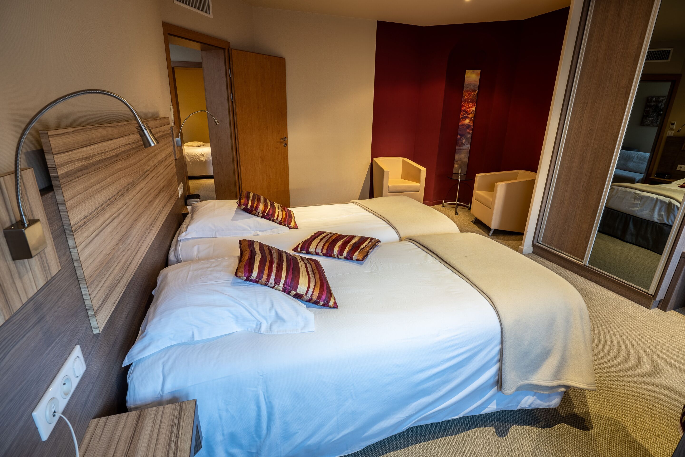 Quarto de hotel com uma cama grande, cabeceira de madeira, uma escrivaninha e uma cadeira.