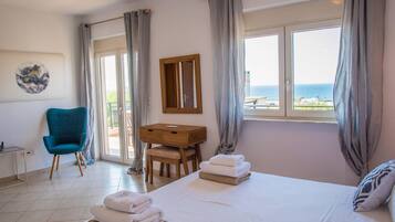 Quarto de hotel com cama, escrivaninha, cadeira e vista para o mar.