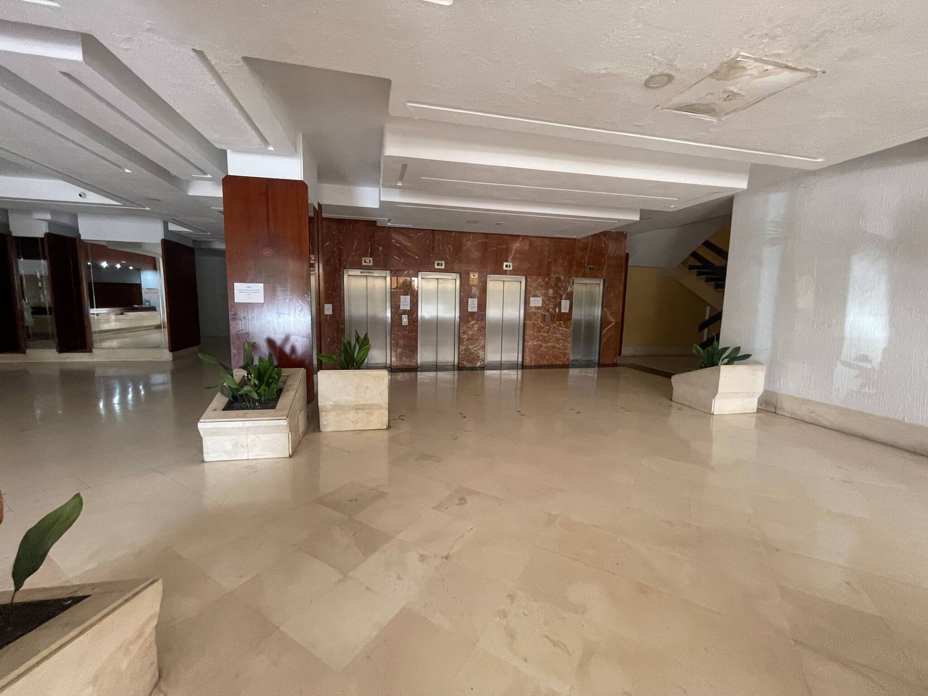 Um hall amplo com piso de mármore, painéis de madeira e três elevadores.