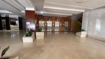 Um hall amplo com piso de mármore, painéis de madeira e três elevadores.