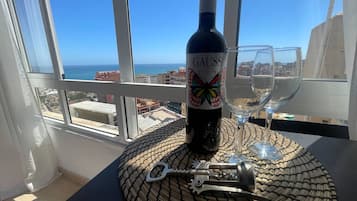 Uma garrafa de vinho Gauss, uma taça de vinho, um abridor de garrafa e uma chave sobre um tapete tecido perto de uma janela com vista para a cidade.