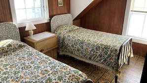 Quarto com duas camas de solteiro, mesa de cabeceira de madeira, abajur e janela com persianas.