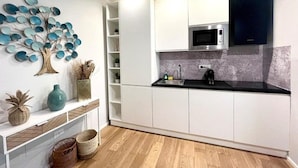 Uma cozinha moderna com armários brancos, bancada preta, micro-ondas de aço inoxidável e uma obra de arte de árvore decorativa na parede.