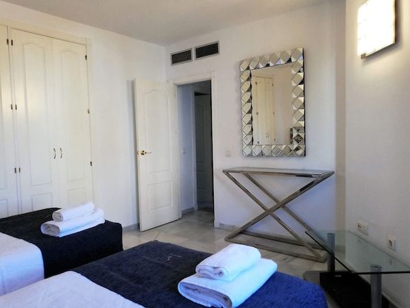 Quarto de hotel com duas camas, um espelho grande, um ferro de passar portátil e uma porta que dá para outro quarto.