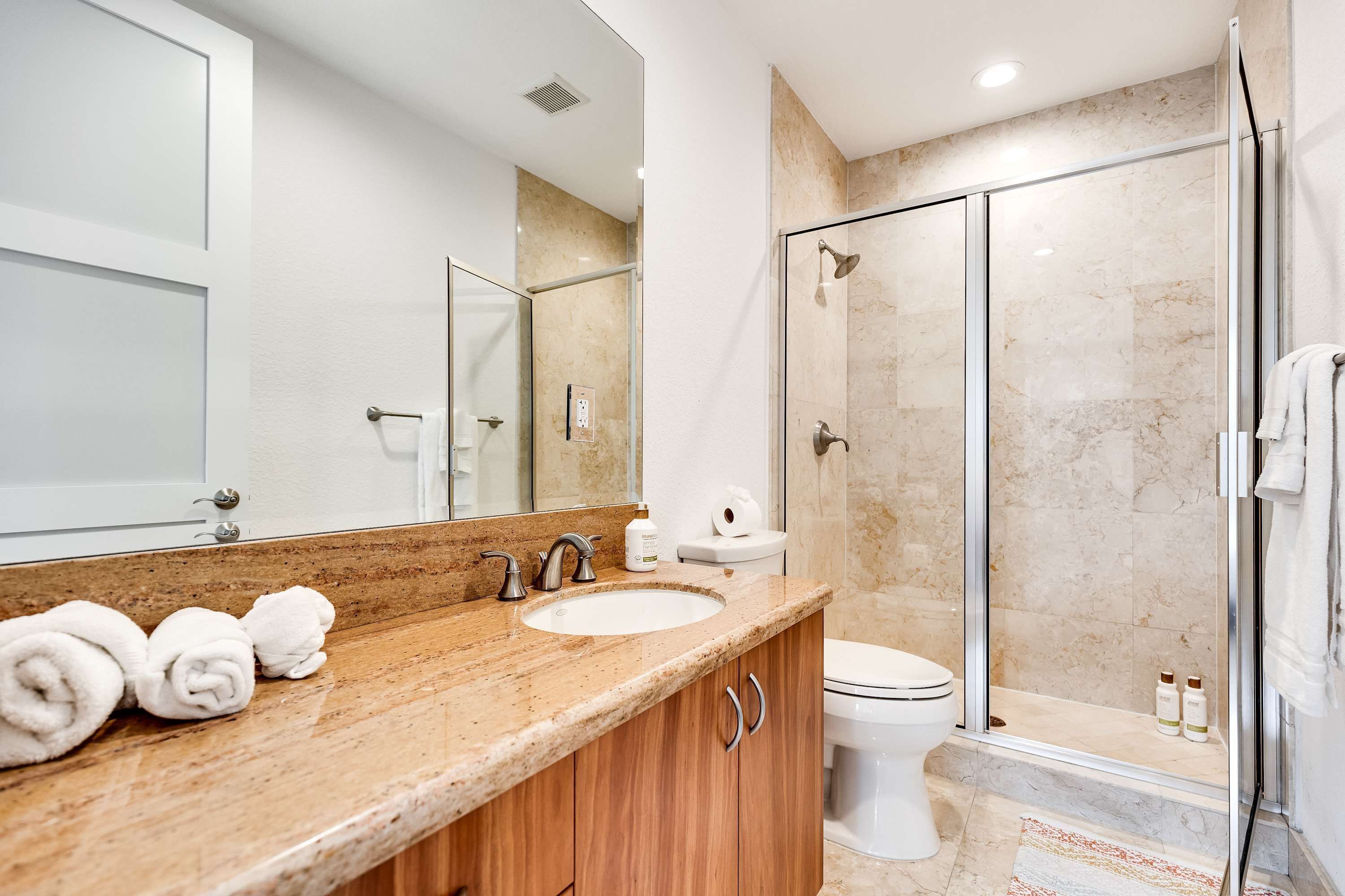 Um banheiro moderno com bancada de mármore, box de vidro e vaso sanitário branco.