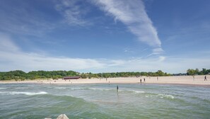 Uma praia com céu limpo, águas calmas e areal arenoso.