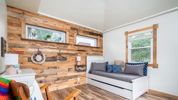 Um quarto acolhedor com parede de madeira, um sofá branco, uma cadeira de madeira e uma pequena mesa com abajur.
