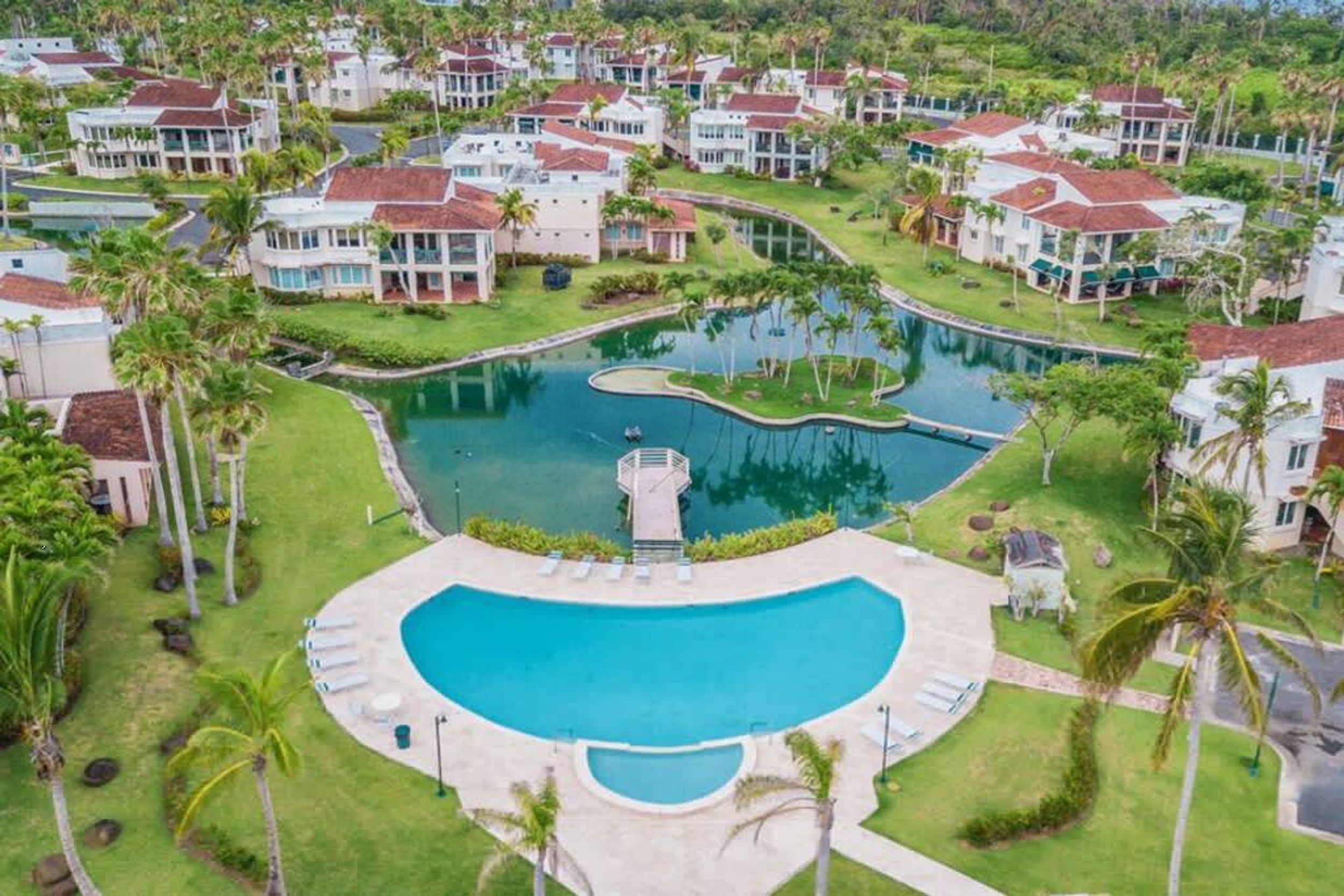 Um resort com piscina central, vários edifícios e vegetação exuberante.