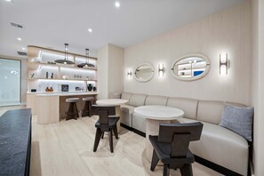 Um saguão de hotel moderno com sofá, mesas redondas, área de bar e espelhos fixados na parede.
