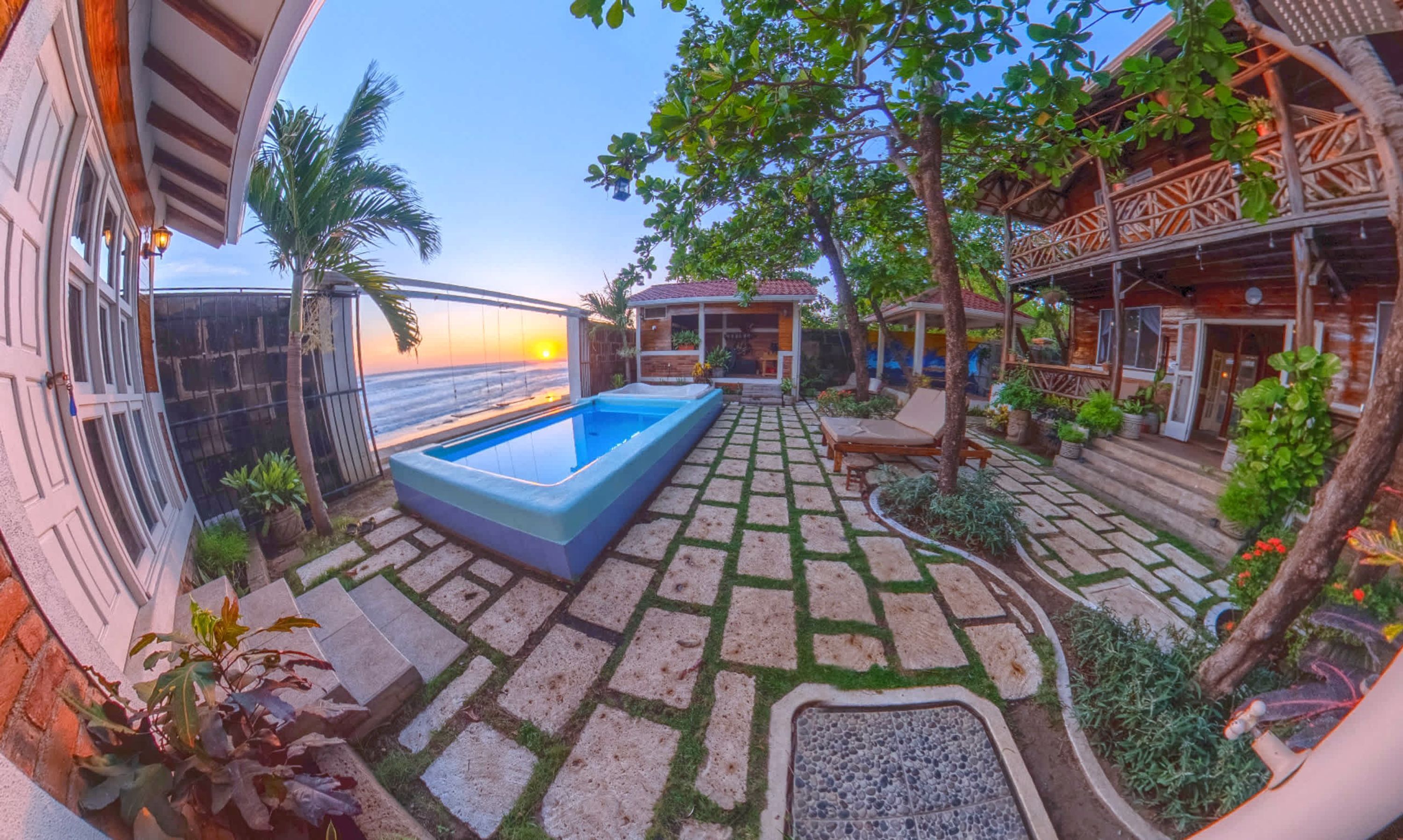 Uma área de piscina com vista para o oceano, rodeada por caminhos de pedra e vegetação.