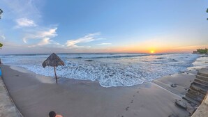 Uma praia com um guarda-sol de palha, ondas e um pôr do sol.